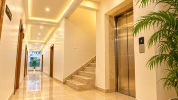 Corredor de hotel com piso de mármore, escada, elevador e planta em vaso.
