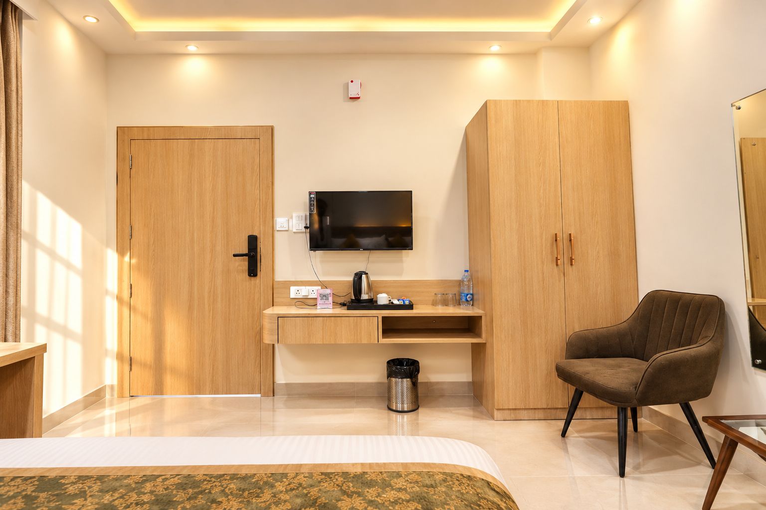 Quarto de hotel com cama, escrivaninha, televisão, cadeira e guarda-roupa.