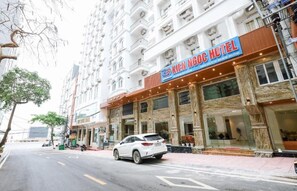 Hotel com placa chamativa, um carro branco estacionado na frente e vista da rua.