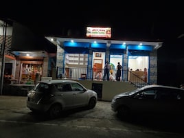 Hotel com fachada azul e letreiro, dois carros estacionados em frente, e entrada visível.