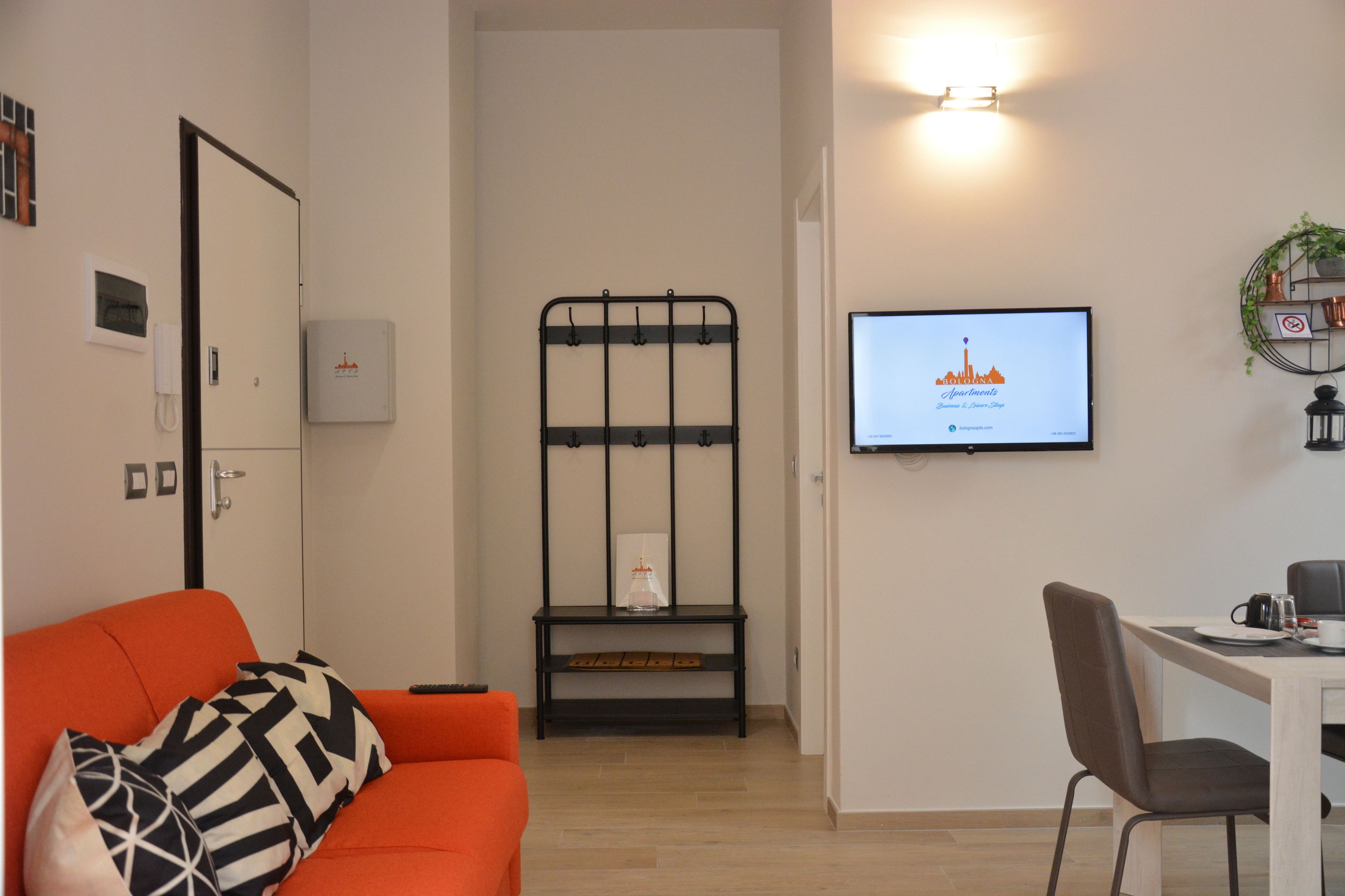 Quarto de hotel com cama, escrivaninha e cadeira, televisão e prateleira com plantas.