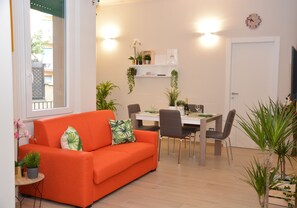 Uma sala de estar moderna com um sofá laranja vibrante, uma mesa de jantar com cadeiras e diversos vasos de plantas.