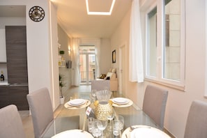Uma sala de jantar com mesa de vidro posta para quatro lugares, cadeiras e vista para a sala de estar.
