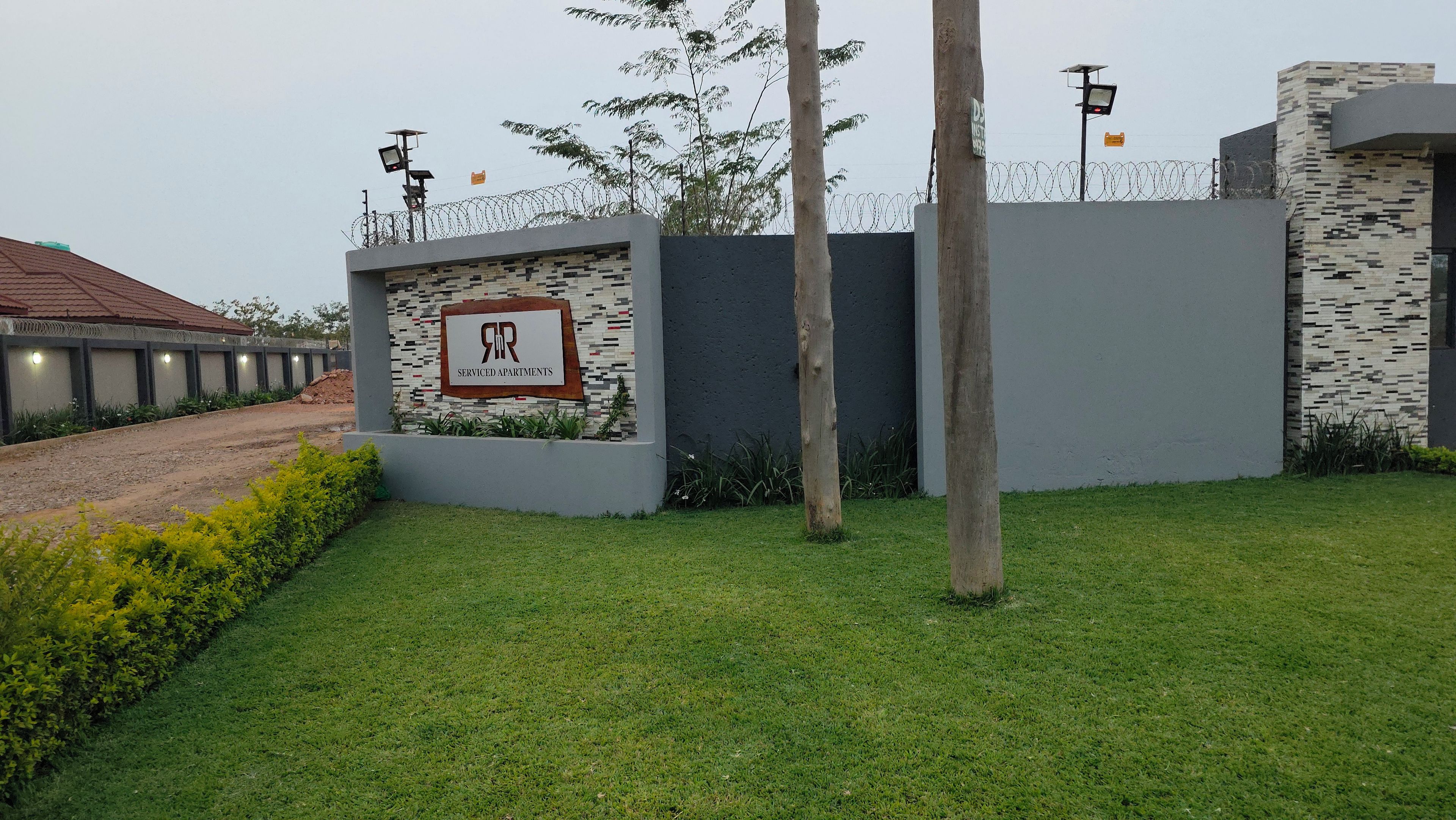 Portão fechado com placa indicando apartamentos com serviço, calçada e gramado bem cuidado.