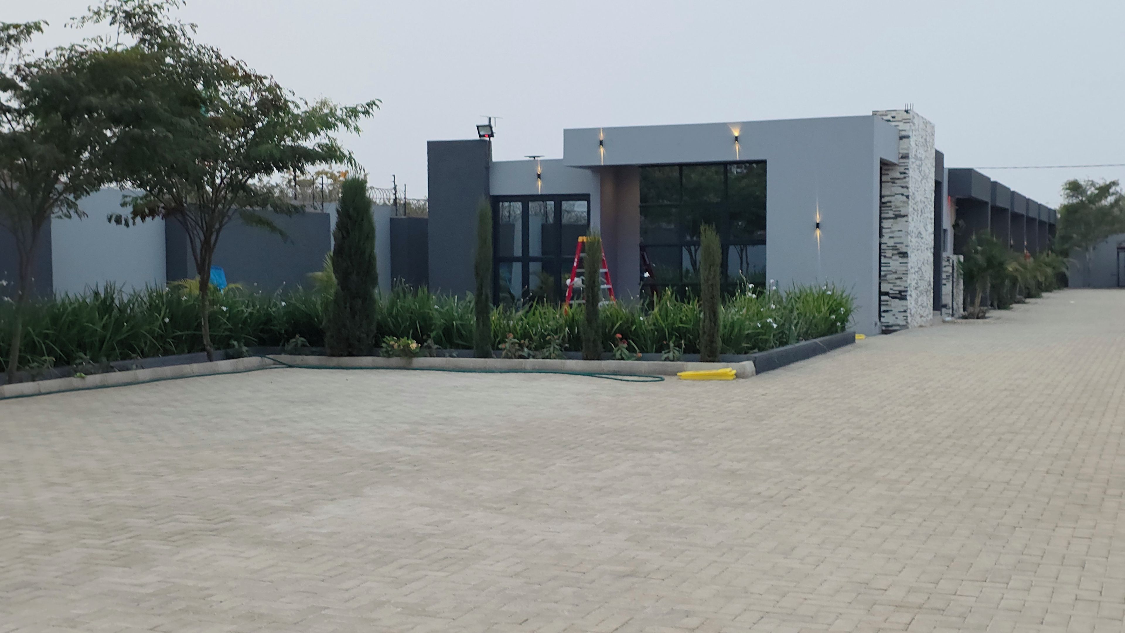 Um edifício moderno com área de entrada pavimentada, uma escada e um jardim bem cuidado.