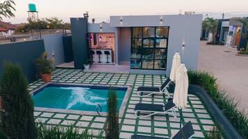 Área de piscina no terraço com espreguiçadeiras, bar e vista da cidade.