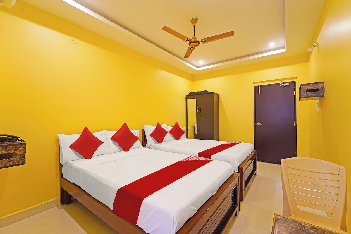 Quarto de hotel com duas camas, um ventilador de teto, um guarda-roupa e uma mesa com cadeira.