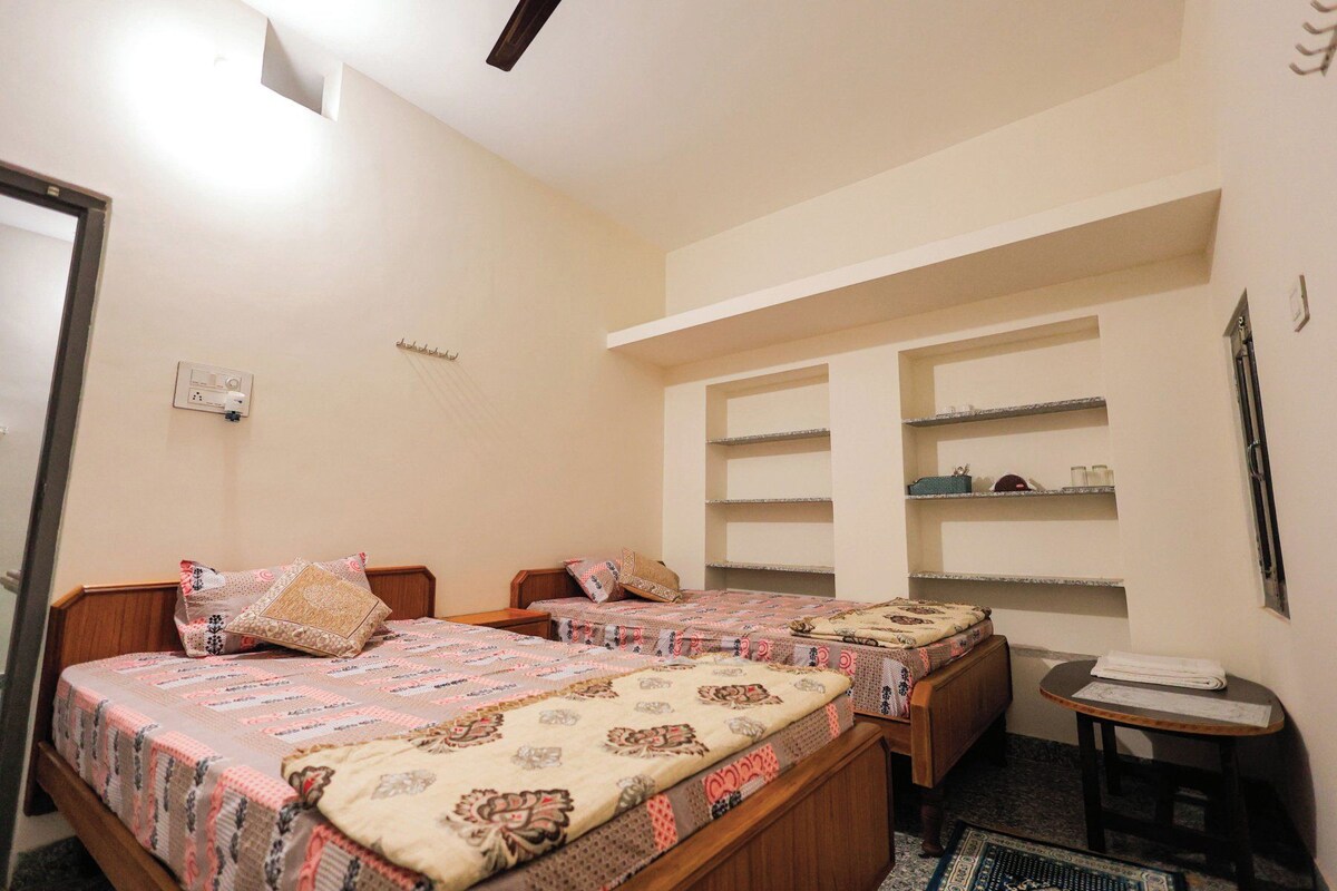 Quarto com duas camas, uma mesa pequena e prateleiras embutidas.