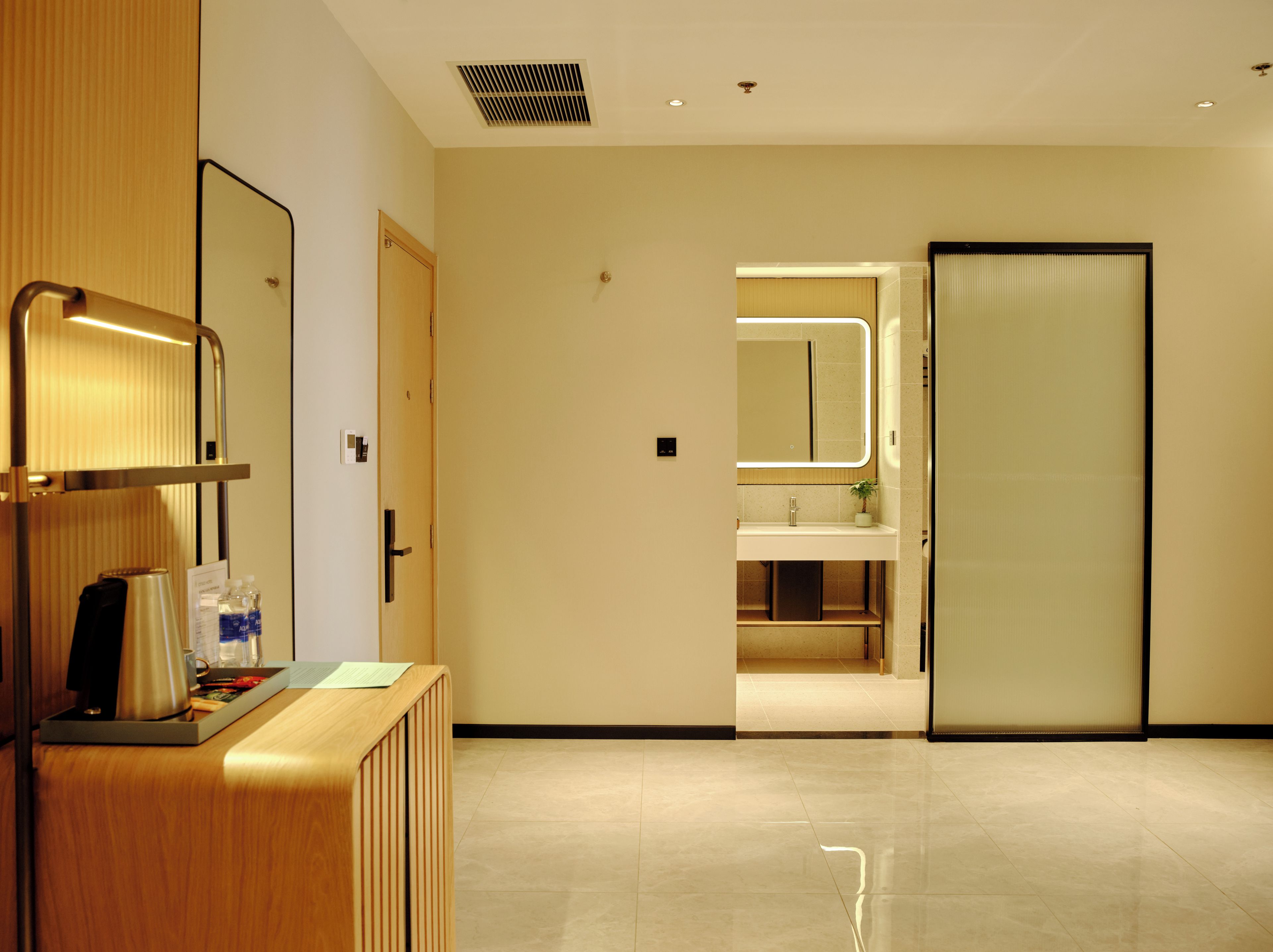 Quarto de hotel com uma receção de madeira, um espelho, uma pia com toalha e uma porta que dá para outro quarto.