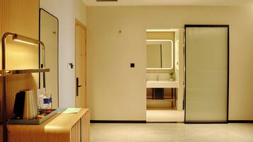 Quarto de hotel com uma receção de madeira, um espelho, uma pia com toalha e uma porta que dá para outro quarto.
