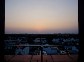 Vista do pôr do sol a partir de uma varanda com vista para uma área residencial, com casas e uma igreja.