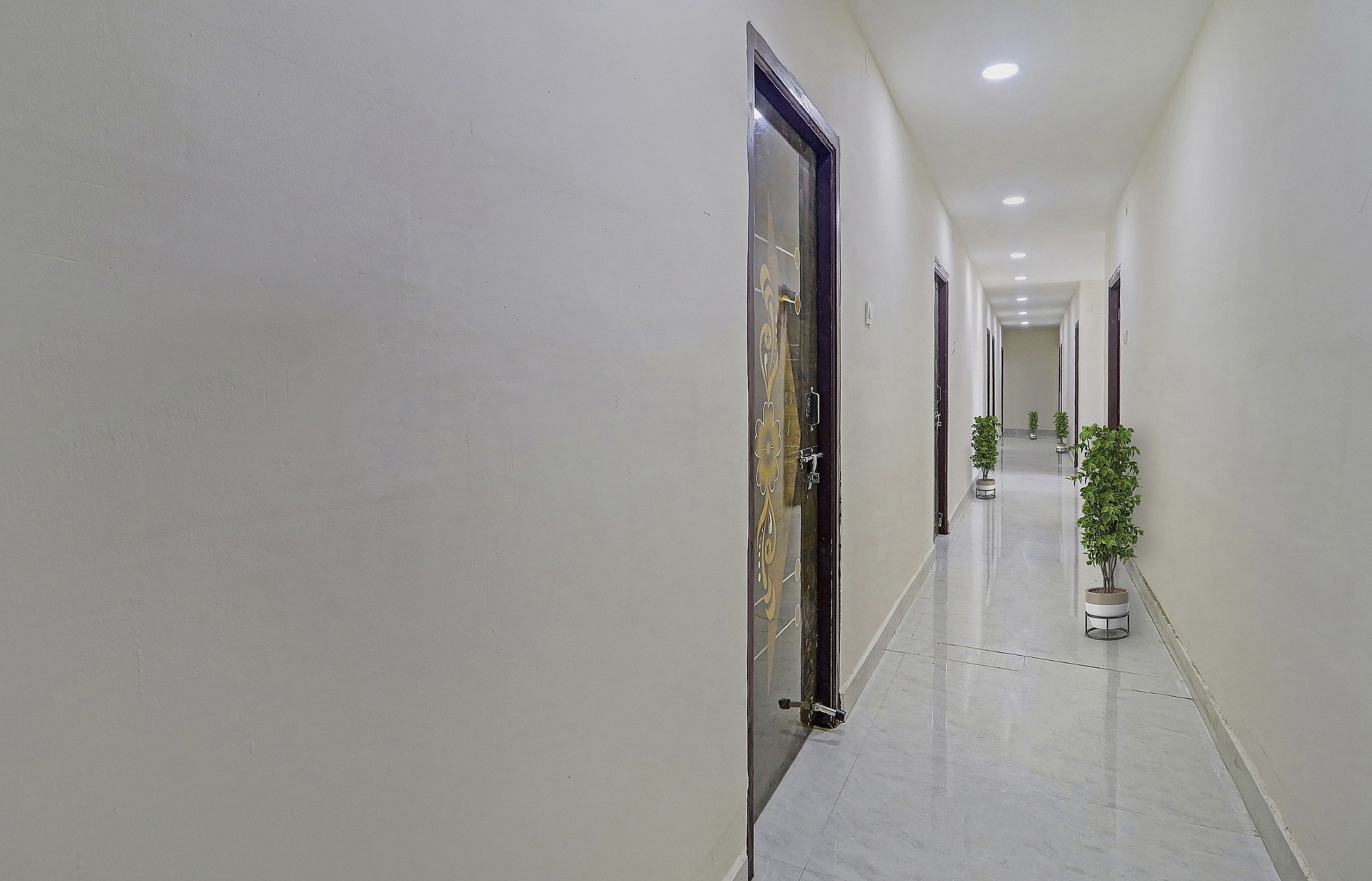 Um corredor com portas em ambos os lados, chão de azulejos e plantas em vasos ao longo da parede direita.