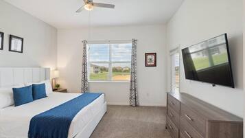 Quarto de hotel com cama, televisão, ventoinha no teto, janela com cortinas e vista para o exterior.