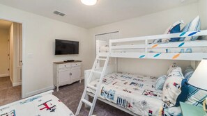Quarto com beliches, televisão, cômoda e escrivaninha com luminária.