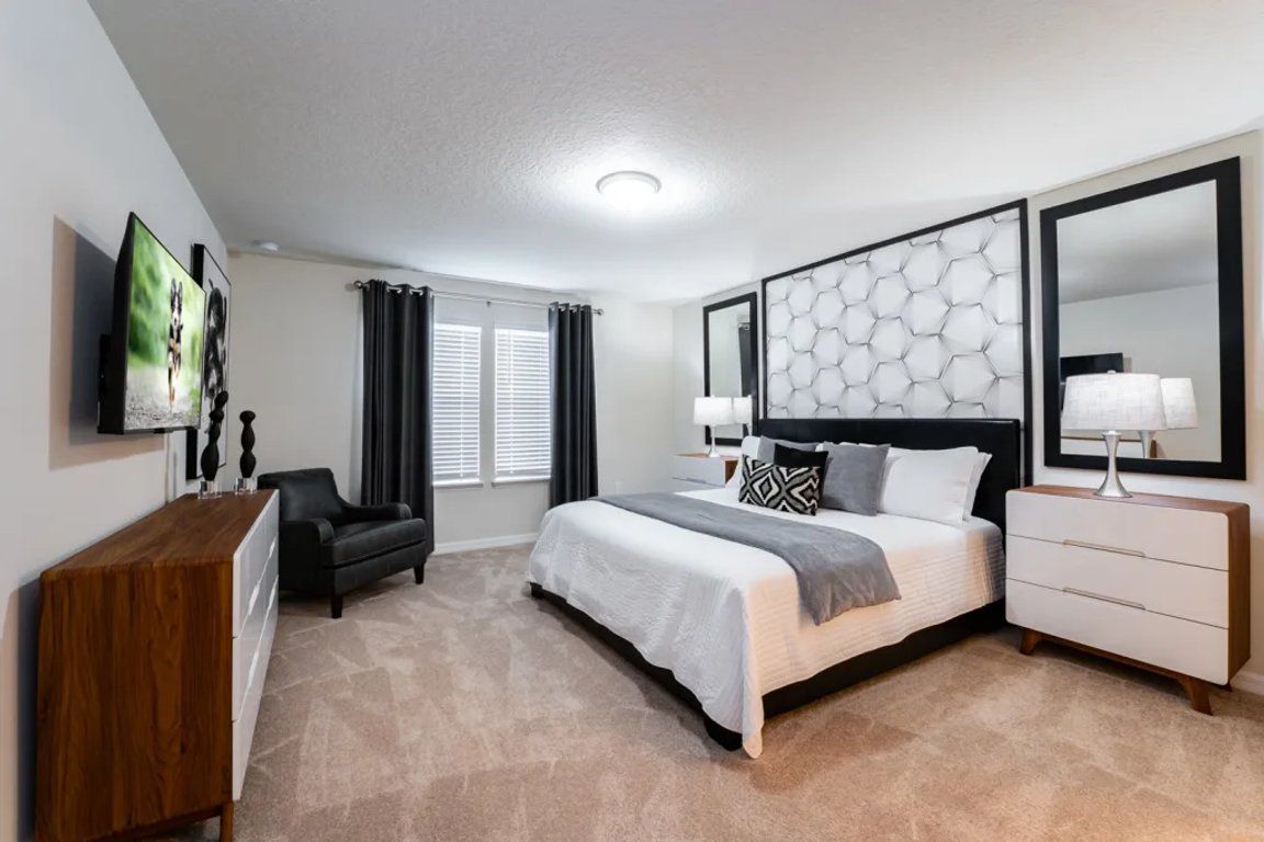 Quarto com cama, mesas de cabeceira, televisão, escrivaninha e cadeira.