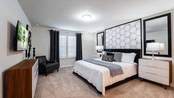 Quarto com cama, mesas de cabeceira, televisão, escrivaninha e cadeira.