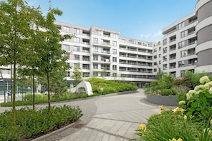 Um edifício residencial moderno com vários andares e varandas, rodeado por jardins ajardinados e árvores.