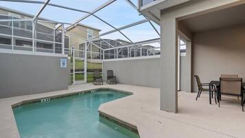 Uma área de piscina com estrutura de vidro, cadeiras e uma mesa.