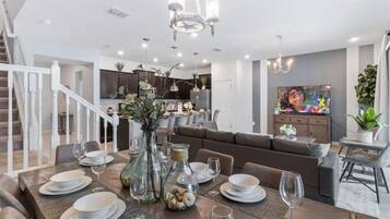 Uma sala de estar moderna com área de jantar, escada e cozinha ao fundo.