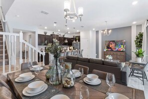 Uma sala de estar moderna com área de jantar, escada e cozinha ao fundo.