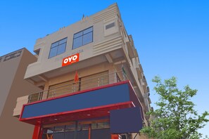 Um edifício de vários andares com uma placa vermelha e branca grande, com a inscrição 'Oyo Rooms'.