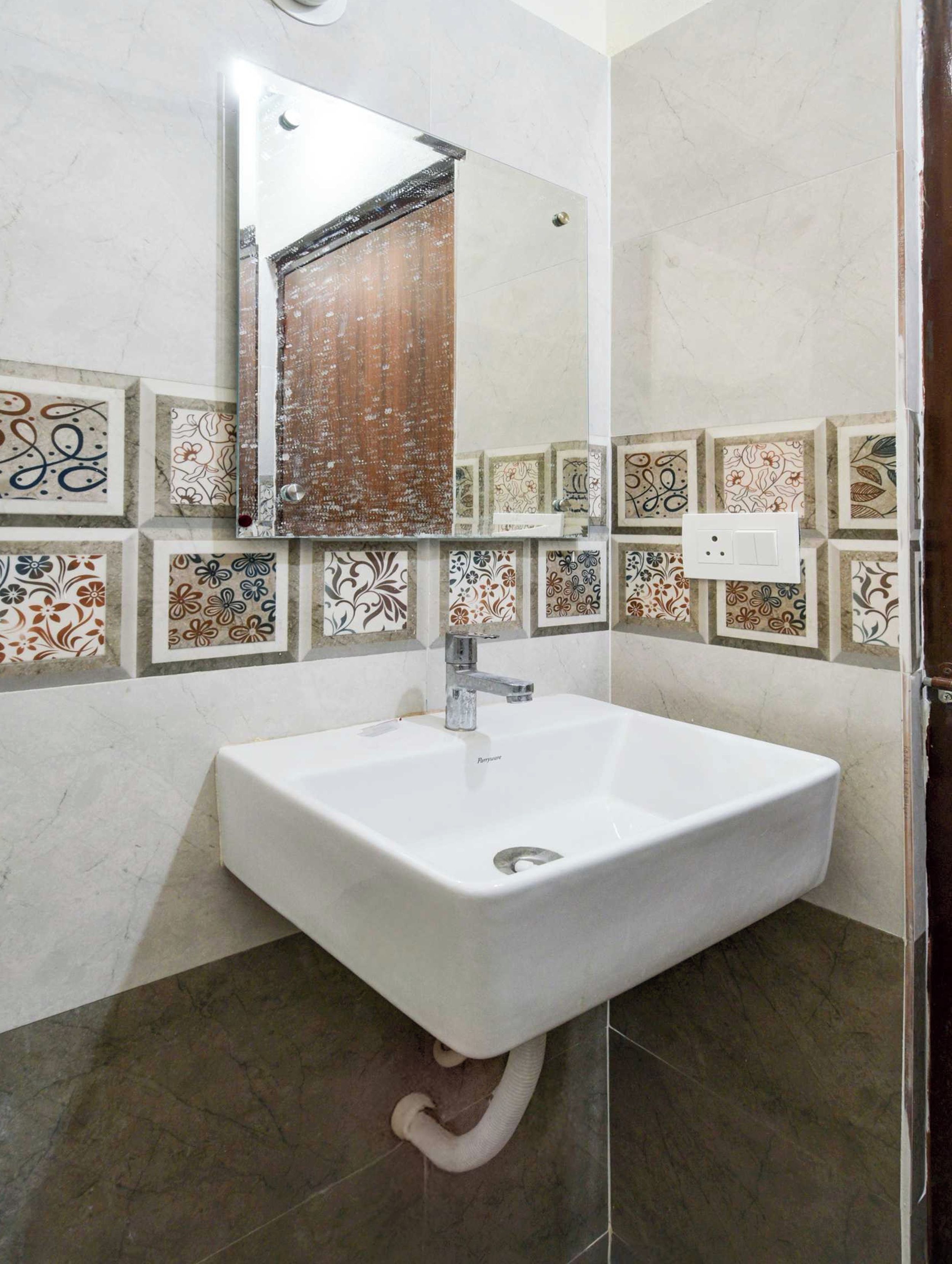 Um banheiro com pia branca, espelho e azulejos estampados nas paredes.