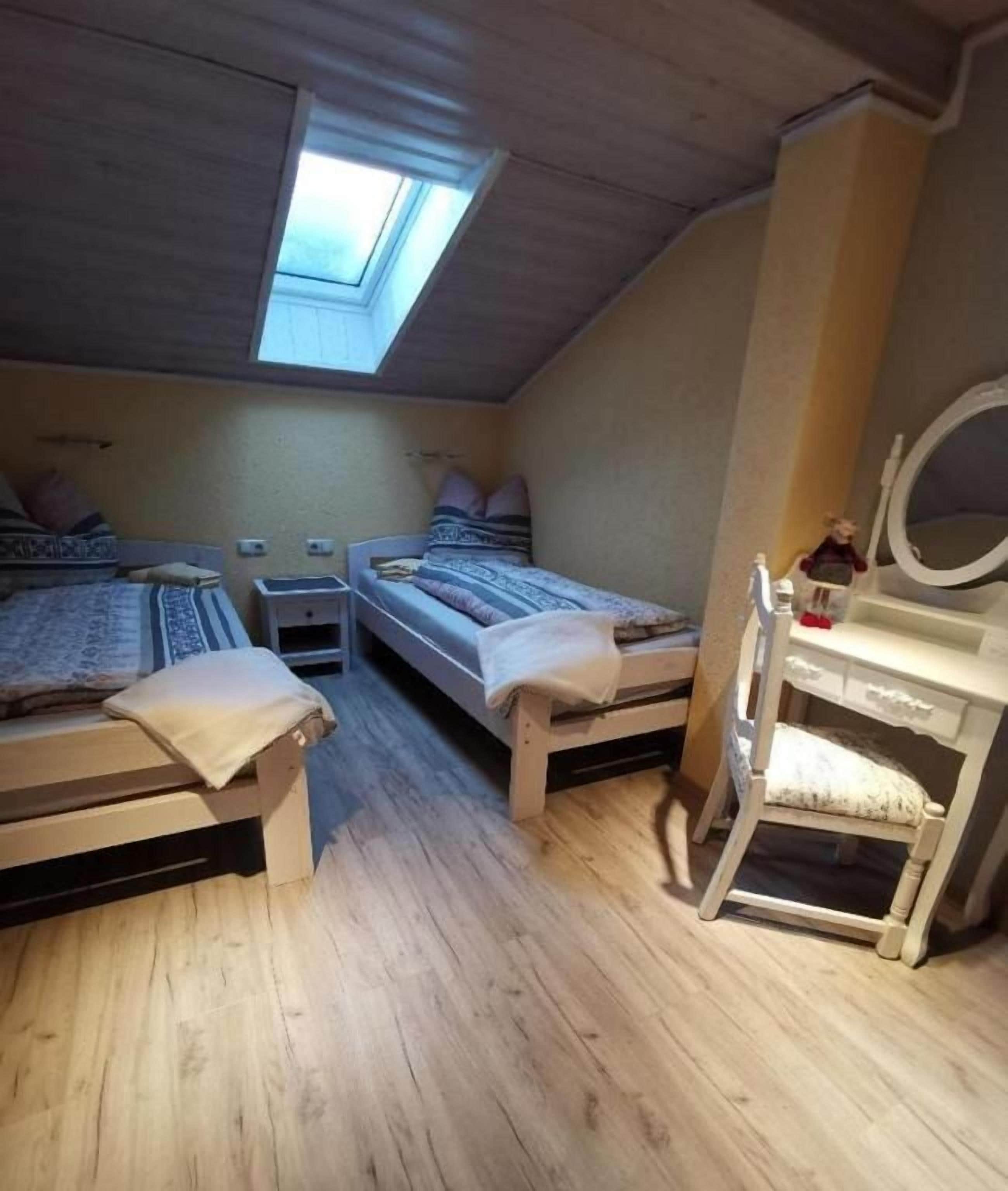 Quarto com duas camas, uma escrivaninha e um claraboia.