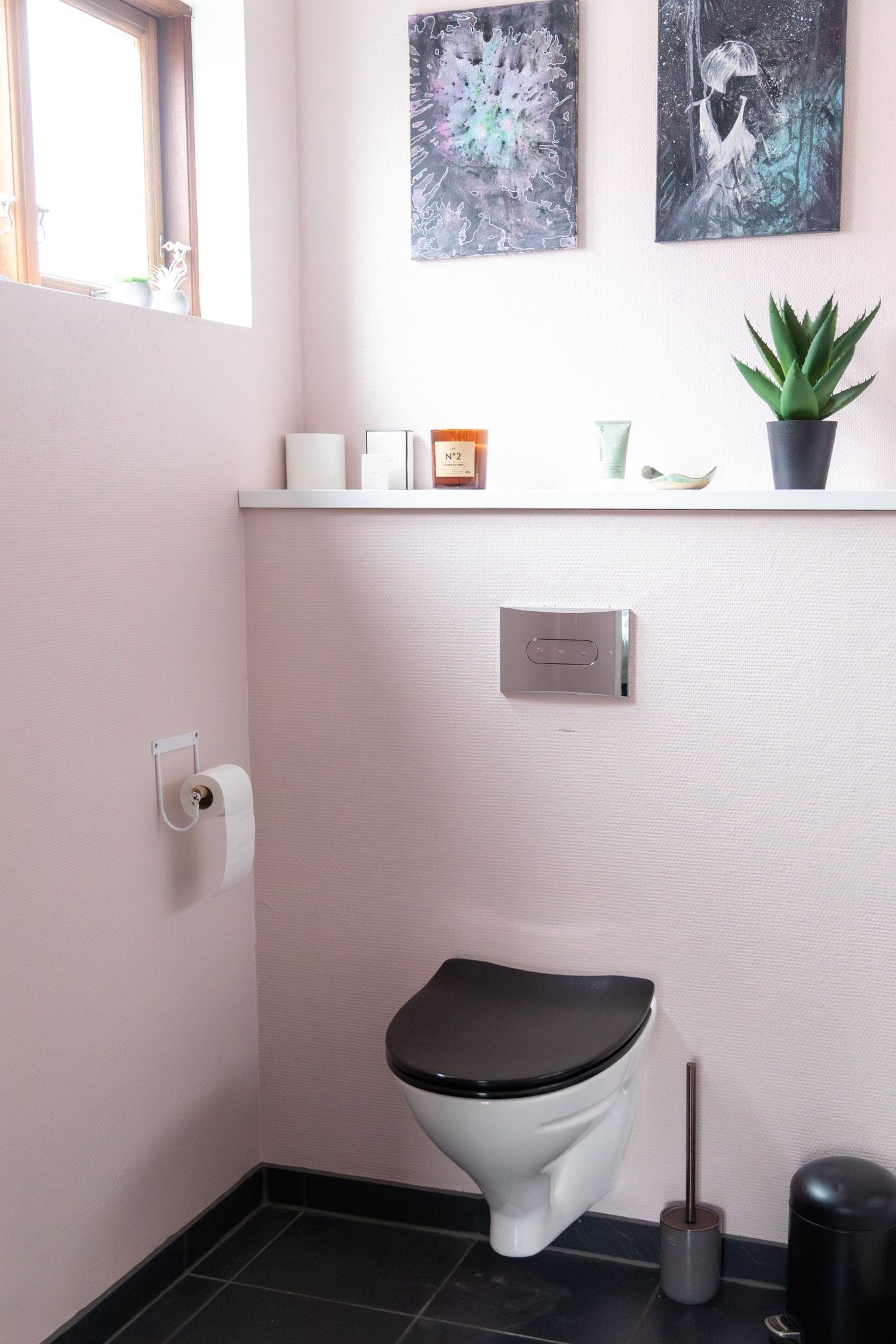 Casa de banho pequena com sanita, secador de mãos, um contentor de lixo e um armário com produtos de higiene pessoal.