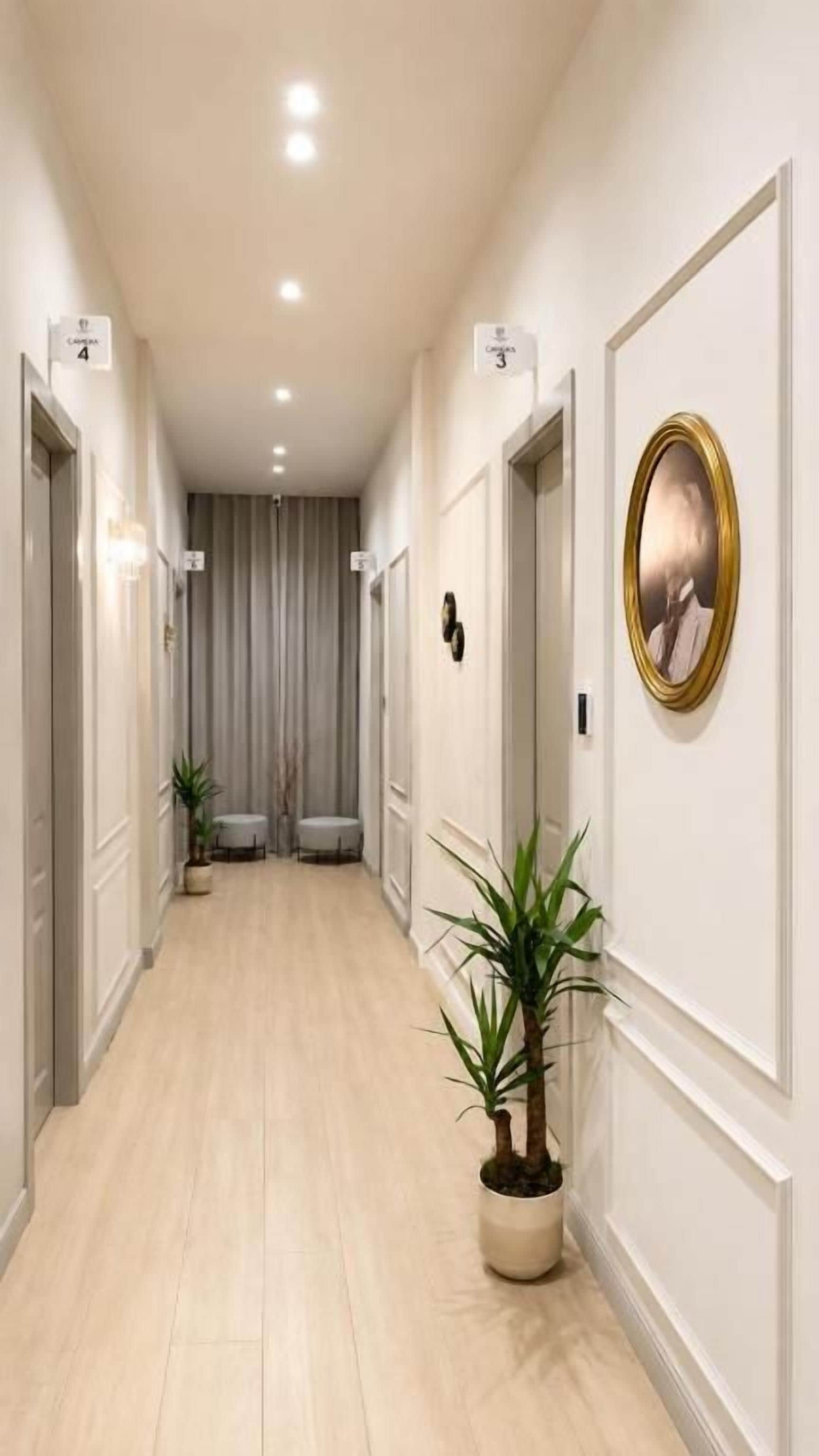 Um corredor com piso de madeira clara, plantas em vasos e um quadro na parede.