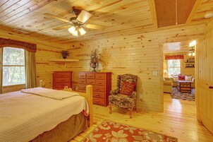 Quarto de cabana de madeira com cama, cômoda, cadeira e uma pequena mesa com um vaso.