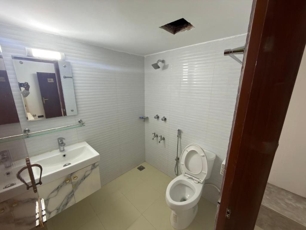 Casa de banho com lavatório branco, espelho e sanita.