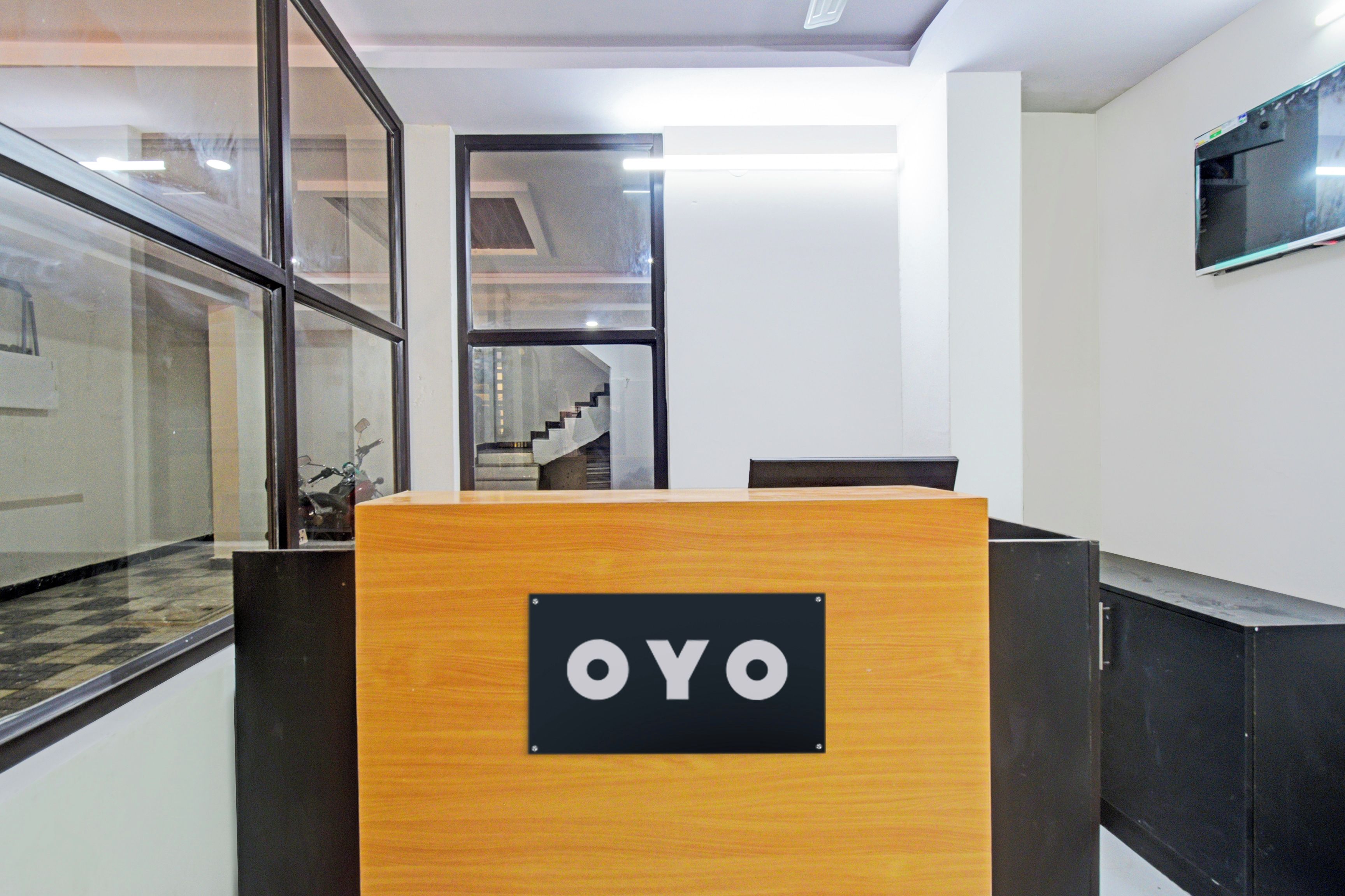 Balcão de recepção com uma placa que diz 'OYO', em um interior moderno com paredes de vidro e uma escada ao fundo.