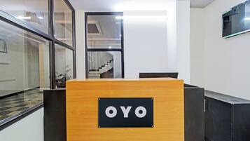 Balcão de recepção com uma placa que diz 'OYO', em um interior moderno com paredes de vidro e uma escada ao fundo.