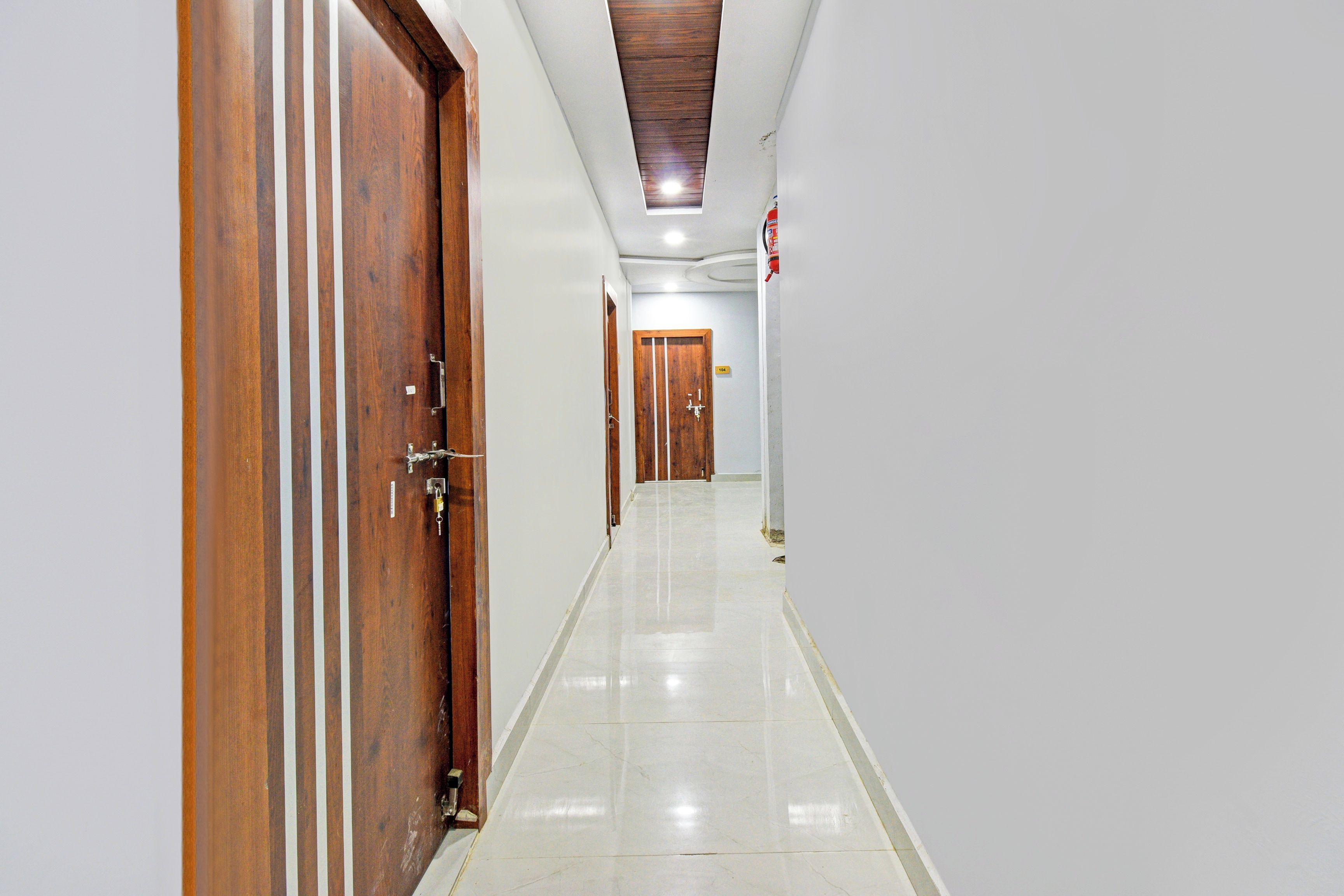 Um corredor com portas de madeira, paredes brancas e chão de azulejos.