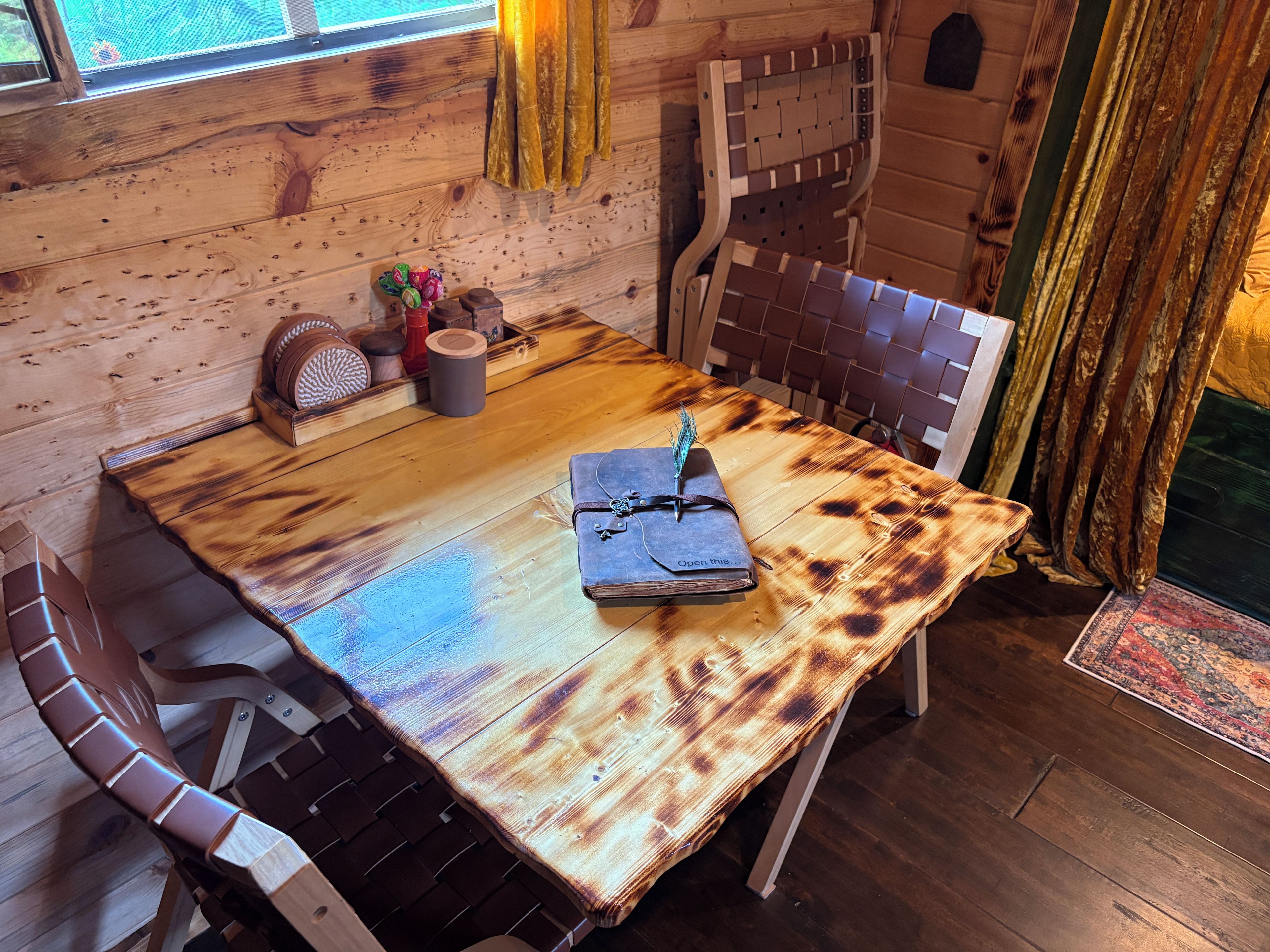 Uma mesa de jantar de madeira com uma cadeira de palha, um livro com uma pena e um objeto decorativo sobre a mesa.