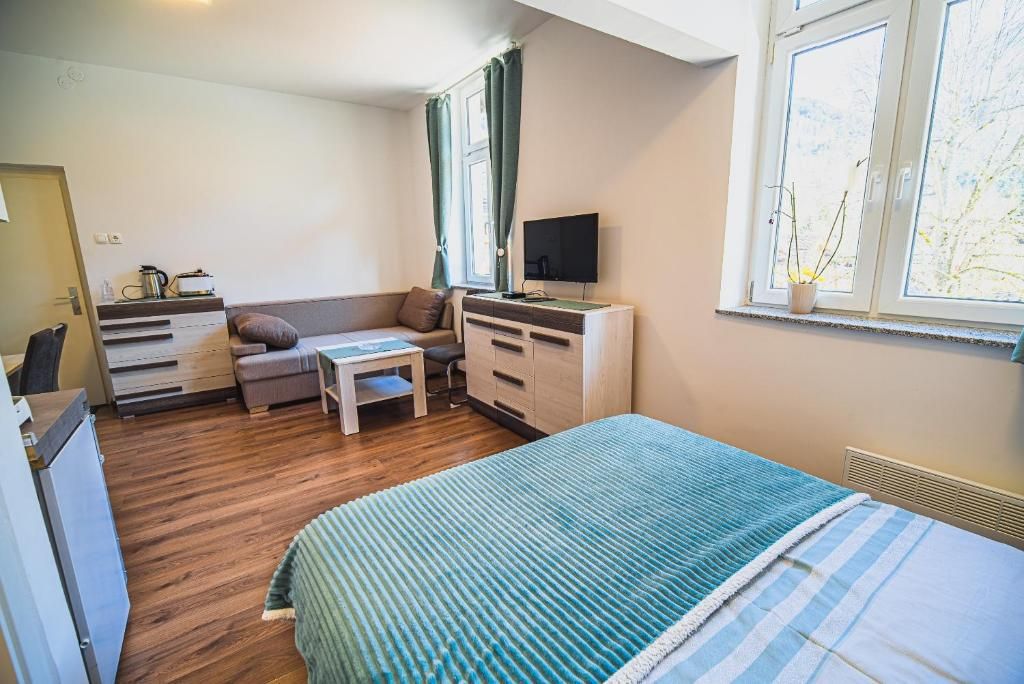 Quarto compacto com cama, escrivaninha, cadeira e televisão.