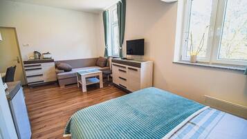 Quarto compacto com cama, escrivaninha, cadeira e televisão.
