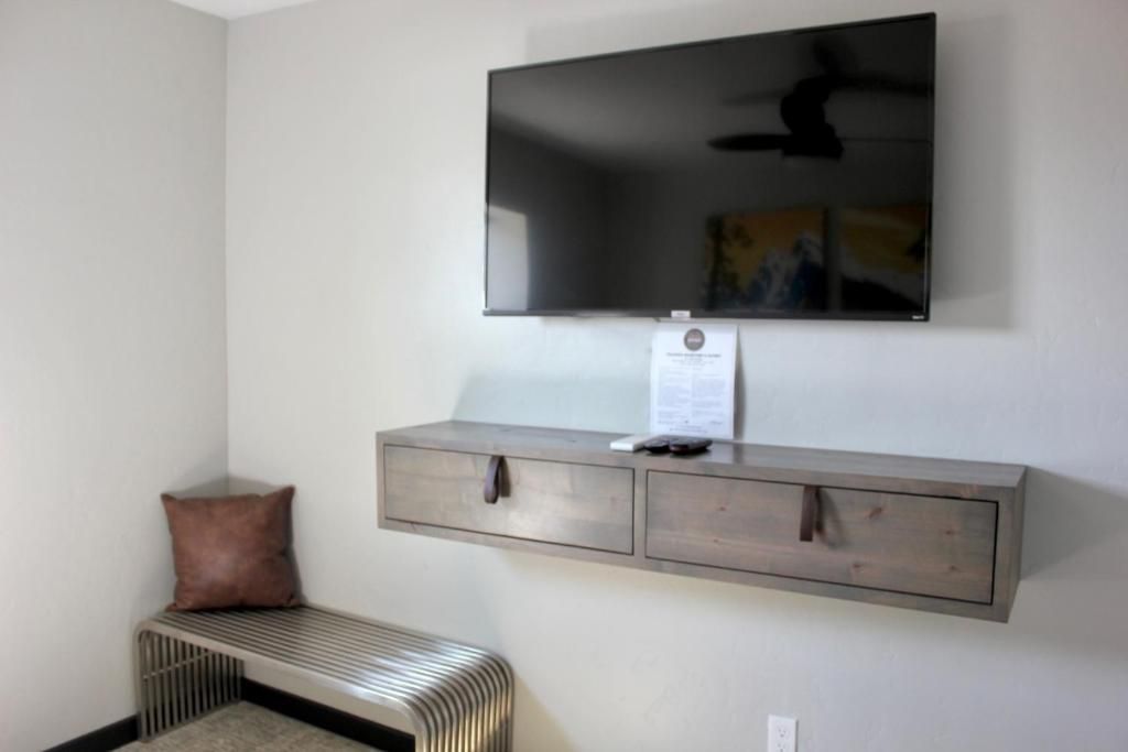 Quarto com televisão de tela plana na parede, um banco de madeira e um pequeno armário com gavetas.
