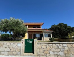 Uma casa de dois andares com uma parede de pedra na frente, uma placa verde com o número 360 e um céu azul límpido.