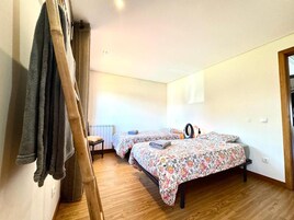 Quarto com duas camas, uma cadeira e um cabideiro.