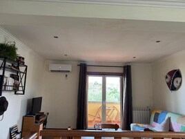 Uma sala de estar com sofá, televisão, estante de livros e janela com cortinas.