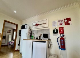 Cozinha compacta com geladeira, micro-ondas e cafeteira. Um extintor de incêndio está fixado na parede.