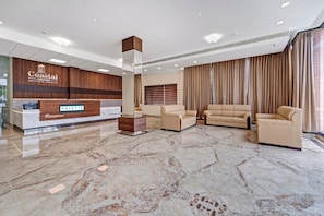 Uma área de recepção com balcão, espaço de estar com sofás e poltronas, e uma grande janela com cortinas.