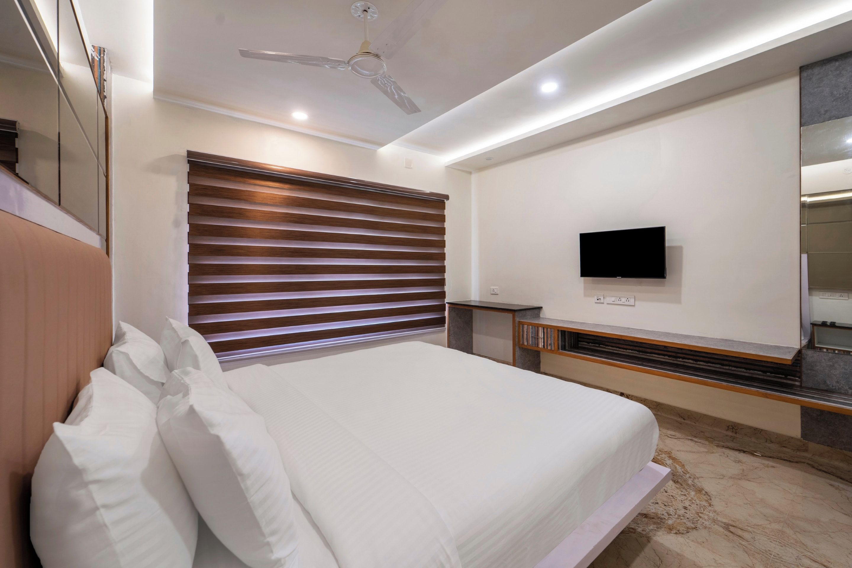 Quarto moderno com cama, TV de tela plana, ventilador de teto e um banco embutido.