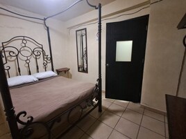 Quarto com cama de dossel, uma mesa de cabeceira pequena, um espelho e uma porta com janela.