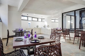 Uma sala de jantar com mesas preparadas para o serviço, cadeiras e um dispensador de água.
