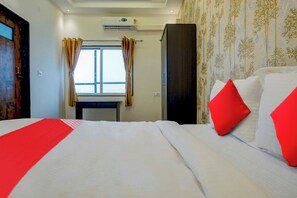 Quarto de hotel com cama, escrivaninha, guarda-roupa e janela com cortinas.