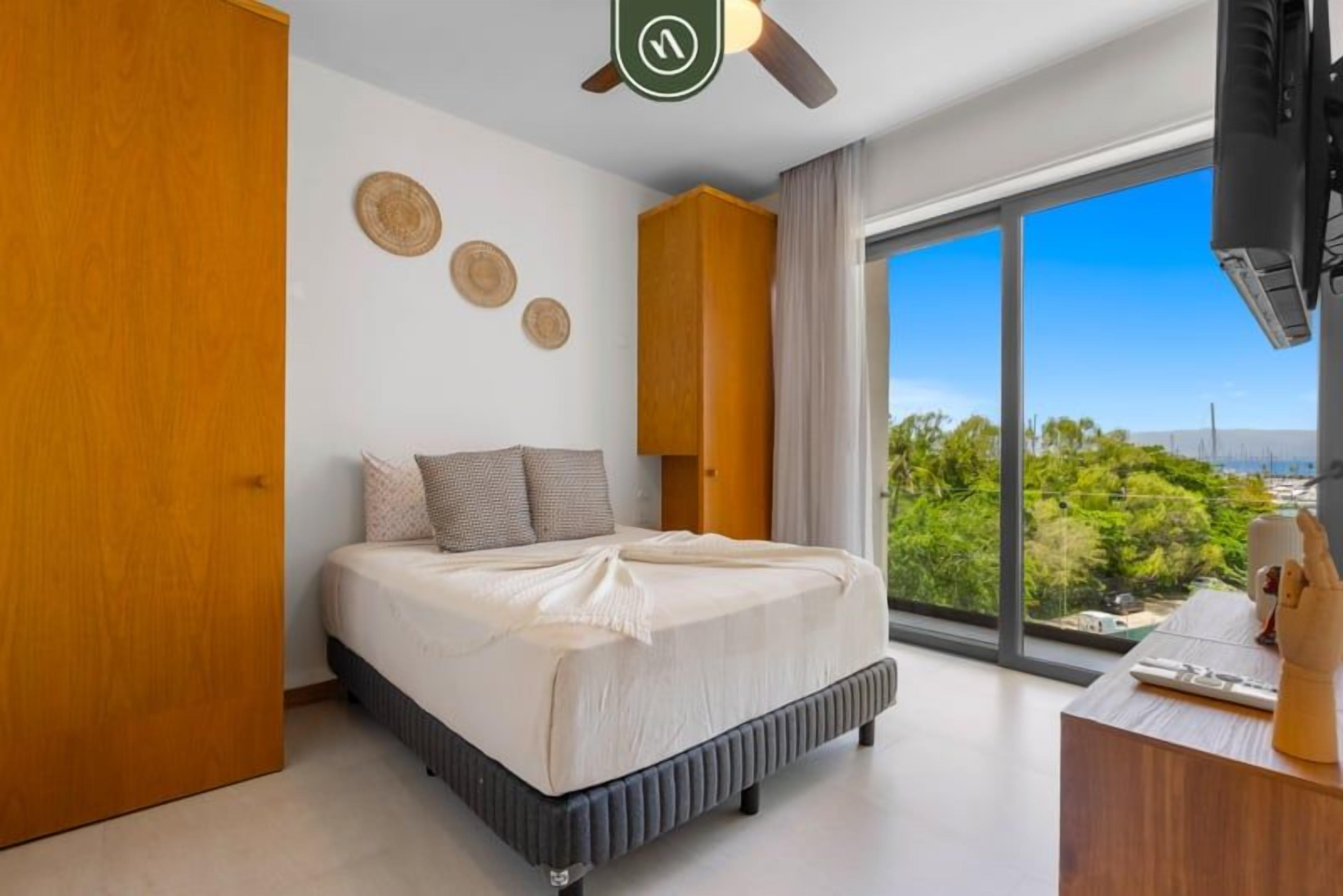 Quarto de hotel com cama, televisão, escrivaninha e uma grande janela com vista.