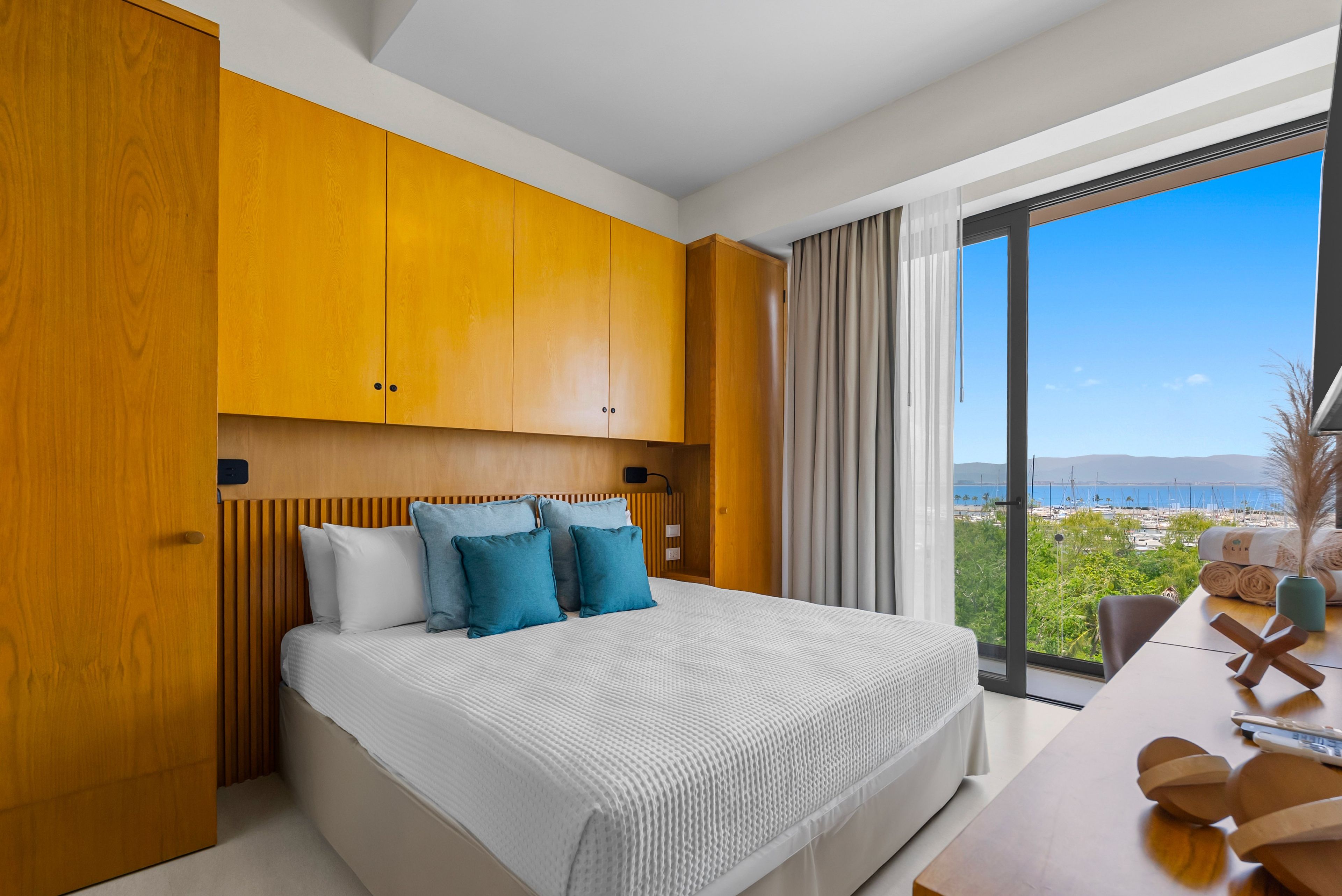 Quarto moderno com uma cama grande, cabeceira de madeira e vista para o mar.