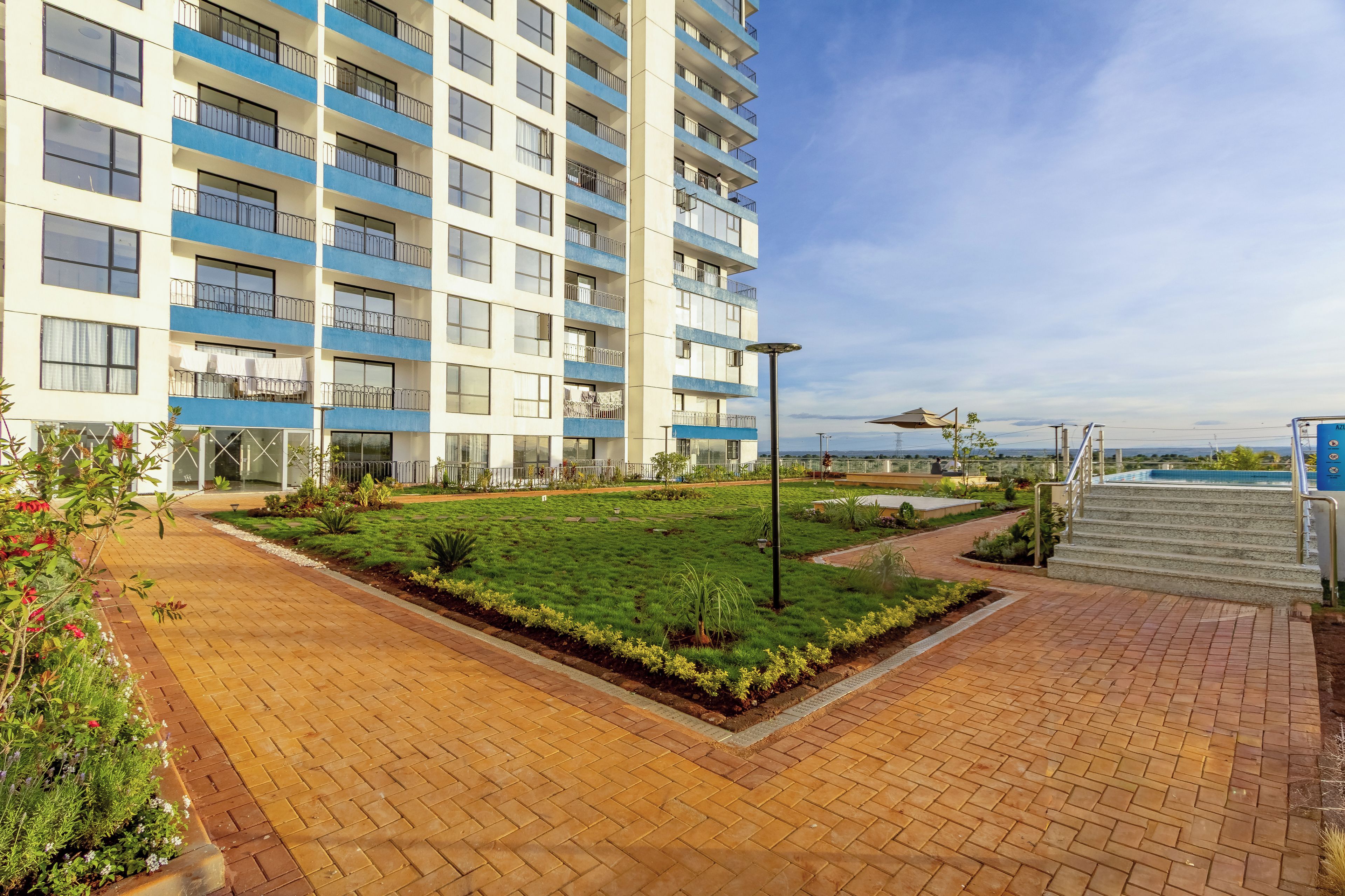 Um edifício residencial com vários andares, varandas, área de jardim ajardinada e piscina ao fundo.